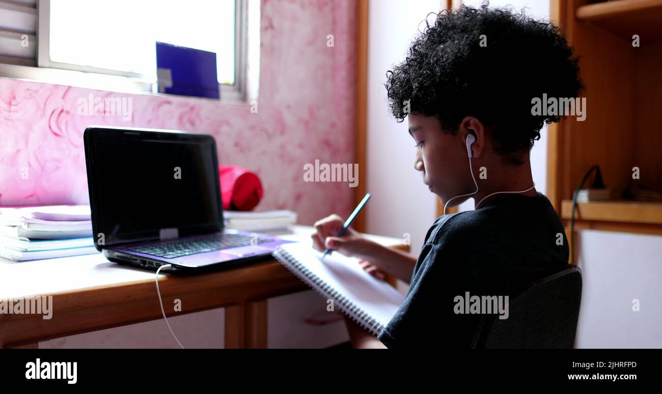 Teen boy studying at home in front of laptop computer. Mixed race kid ...