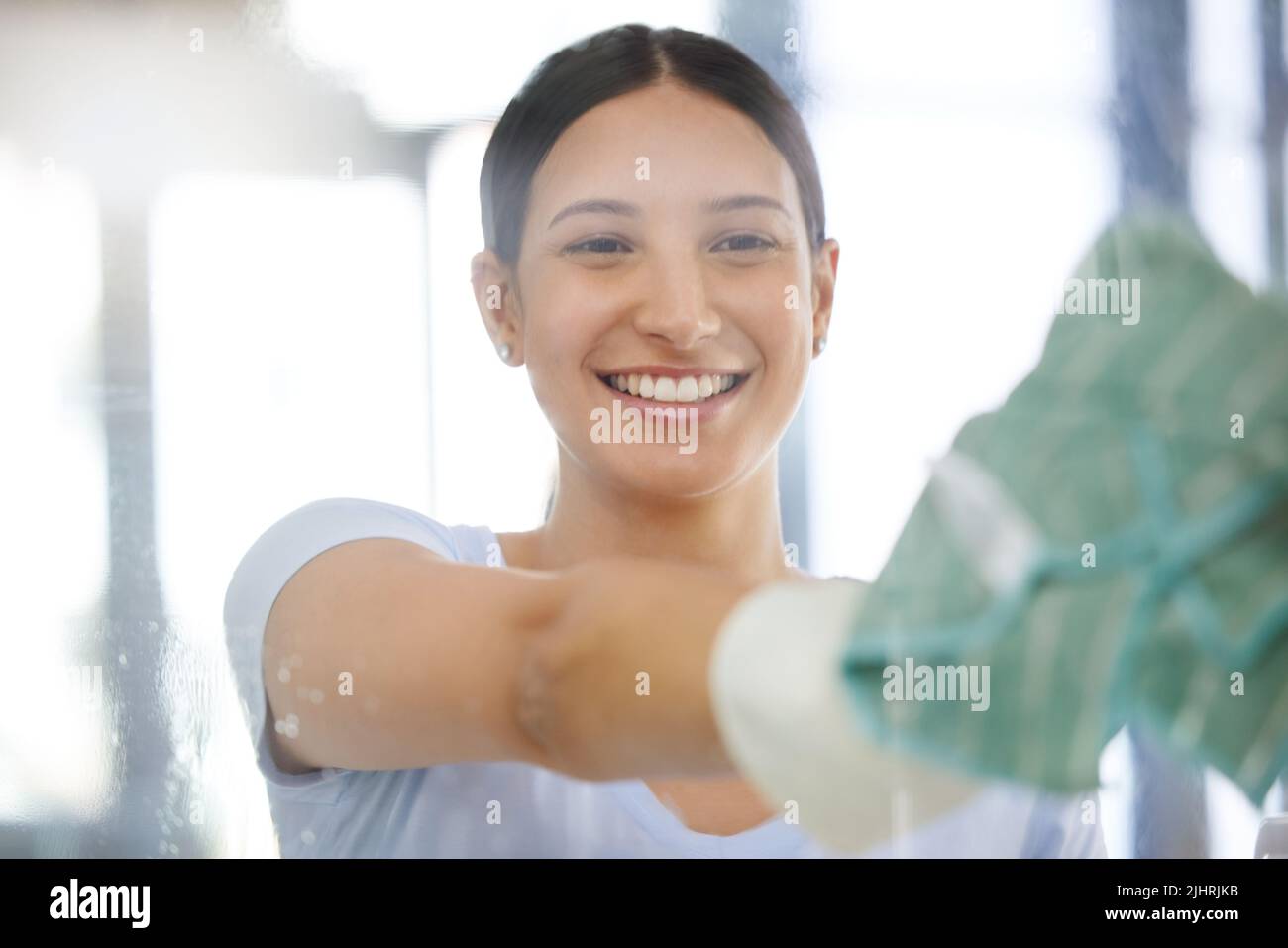 Portrait of a happy mixed race domestic worker using a cloth on a ...