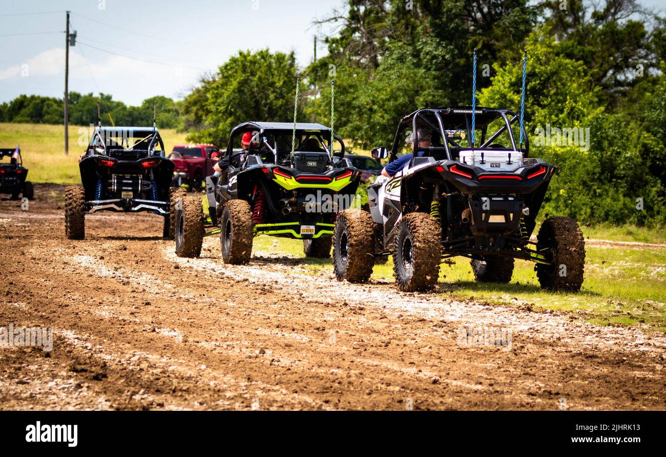 A row of ATVs with people driving around and racing on a dirty muddy field at Rock Fest in 2020 ...
