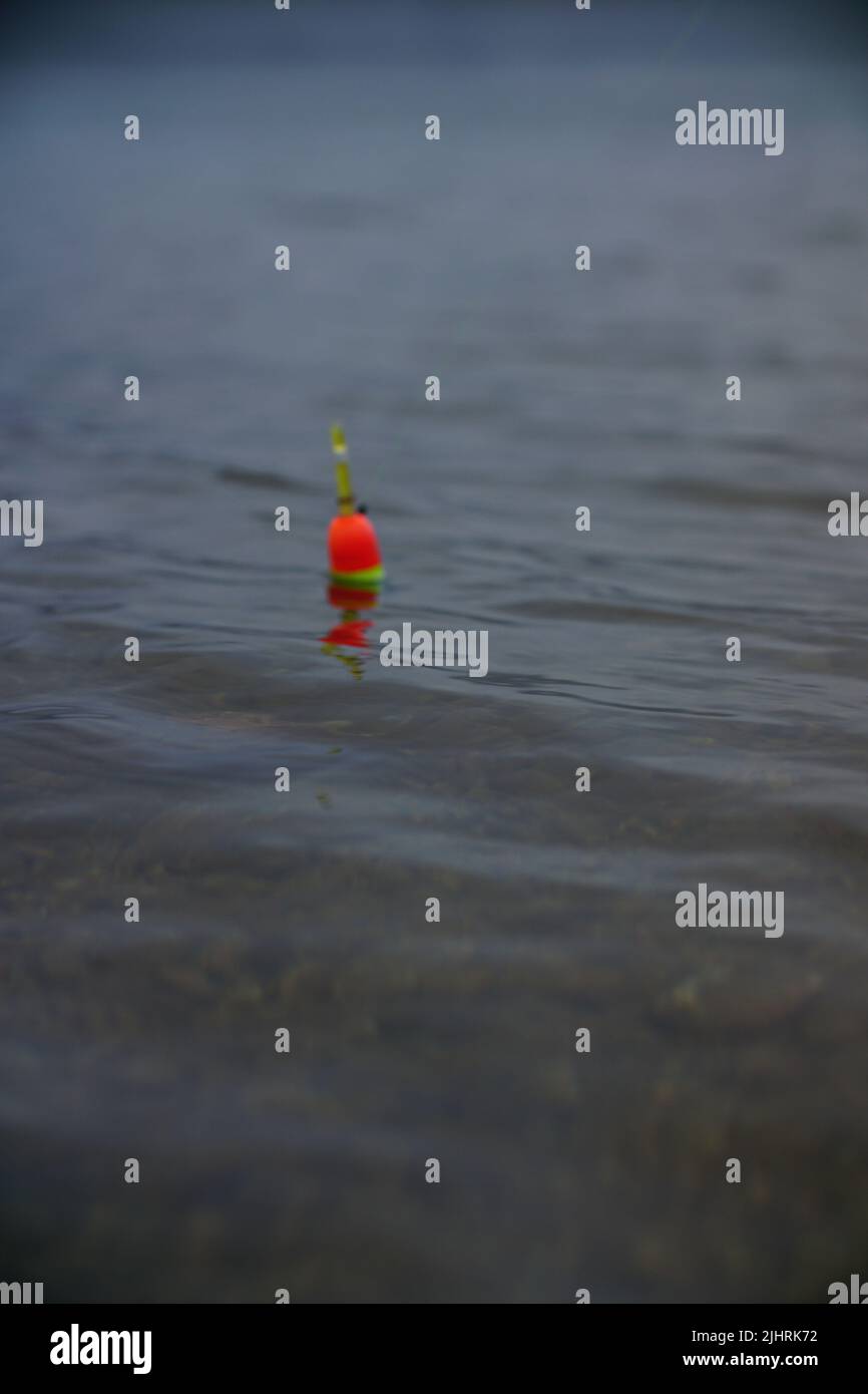 A vertical shot of orange and green fishing bobber floating in the ...