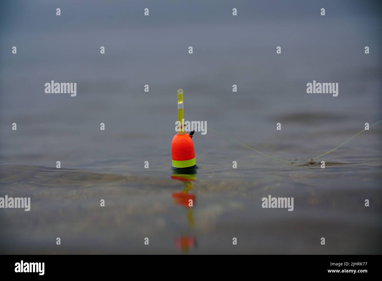An orange and green fishing bobber floating in the water Stock Photo ...