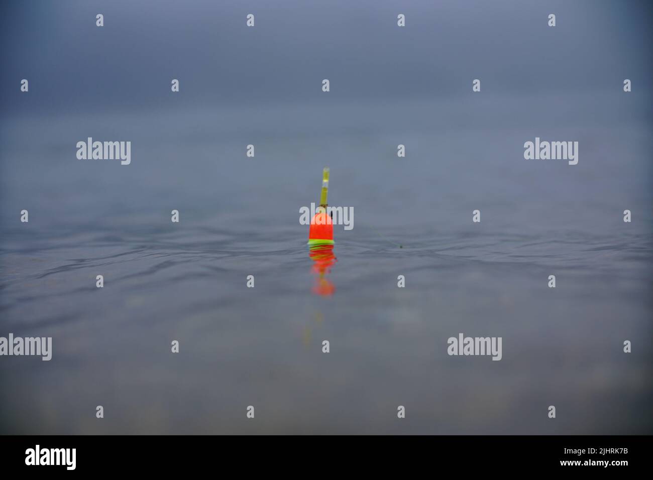 An orange and green fishing bobber floating in the water Stock Photo ...