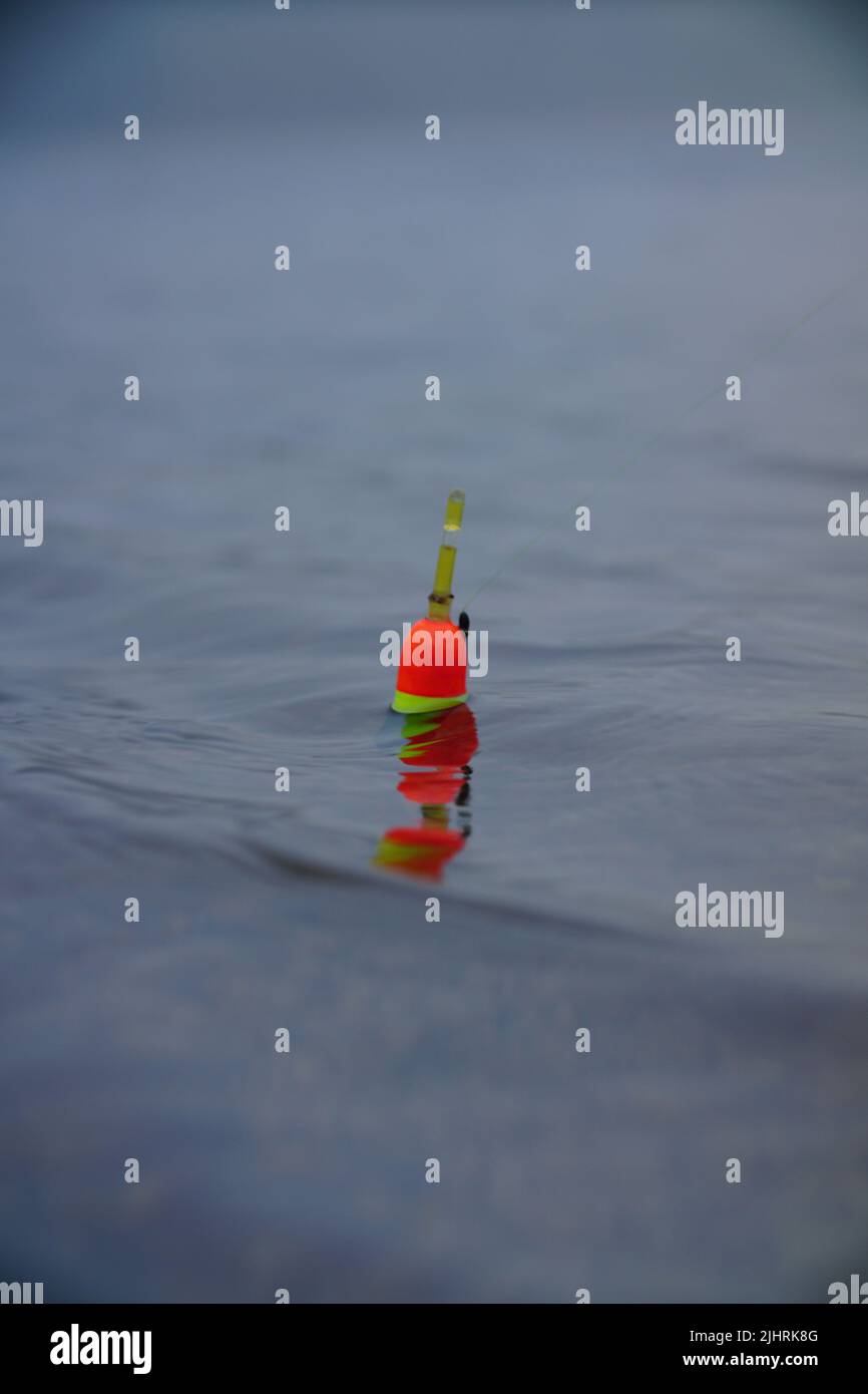 A vertical shot of orange and green fishing bobber floating in the ...