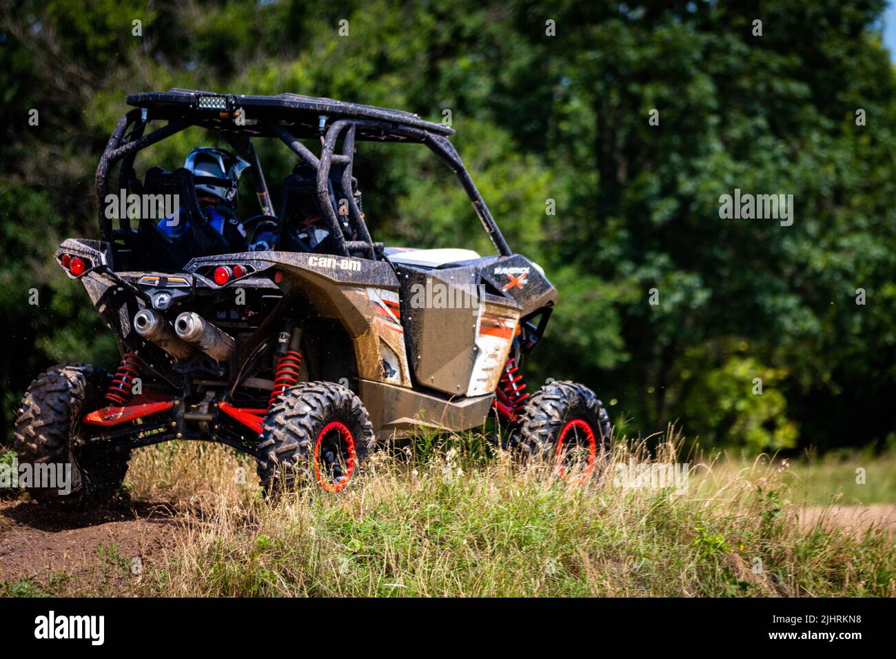 A rear view of drivers in a side-by-side vehicle (UTV) on a dirt track ...