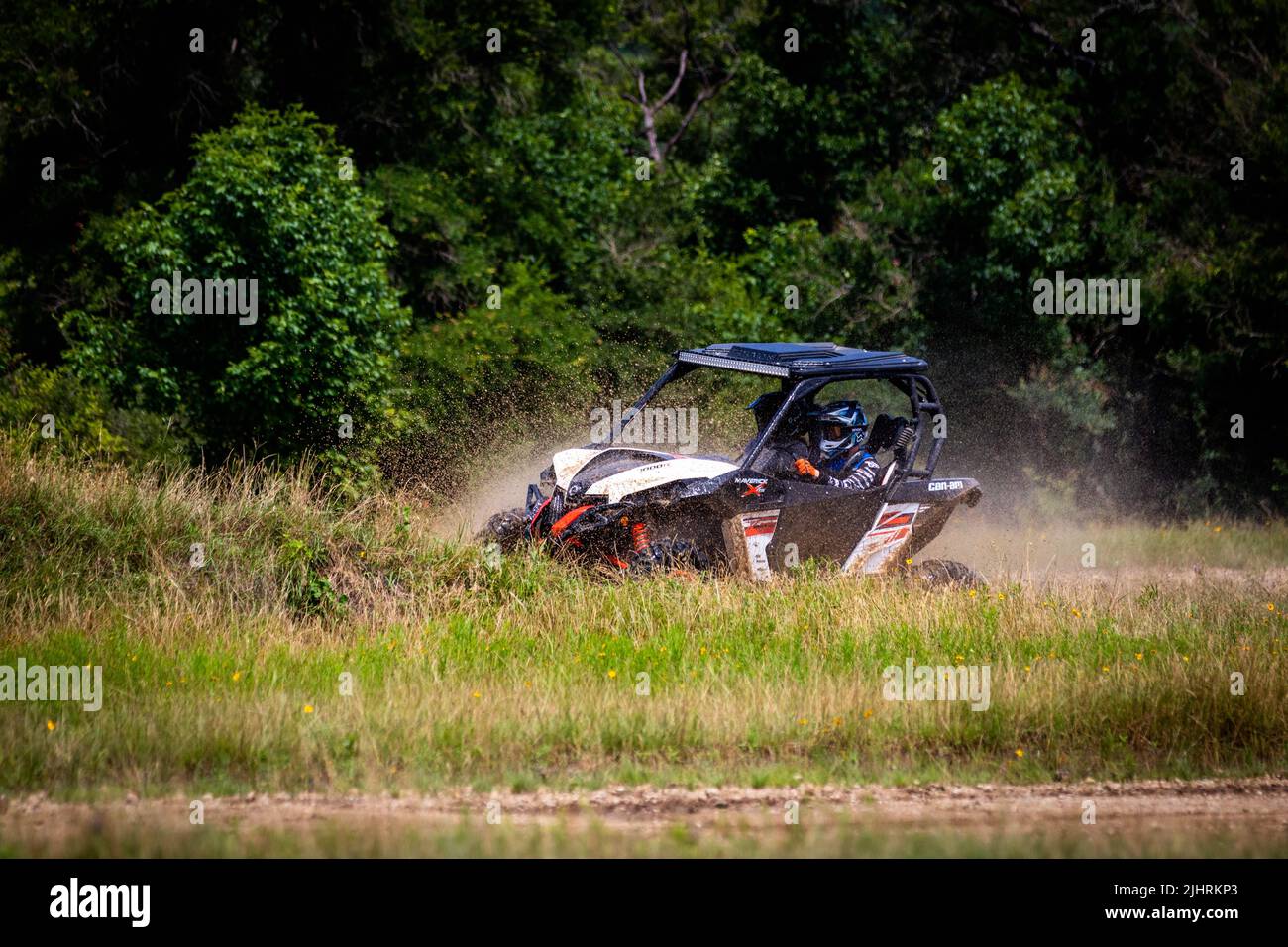 A closeup of drivers in a side-by-side vehicle (UTV) splashing mud on a ...