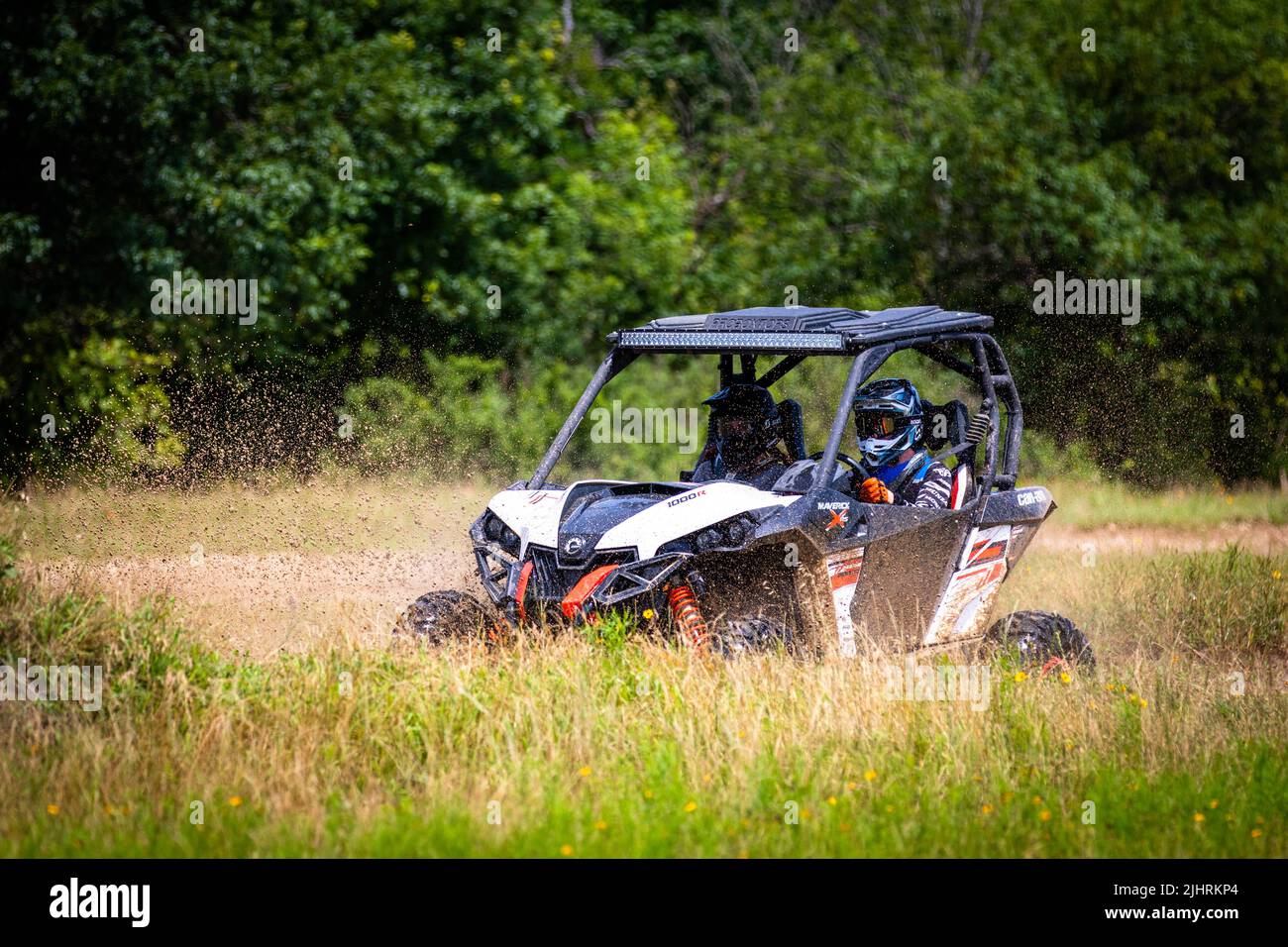 A closeup of drivers in a side-by-side vehicle (UTV) on a dirt track ...
