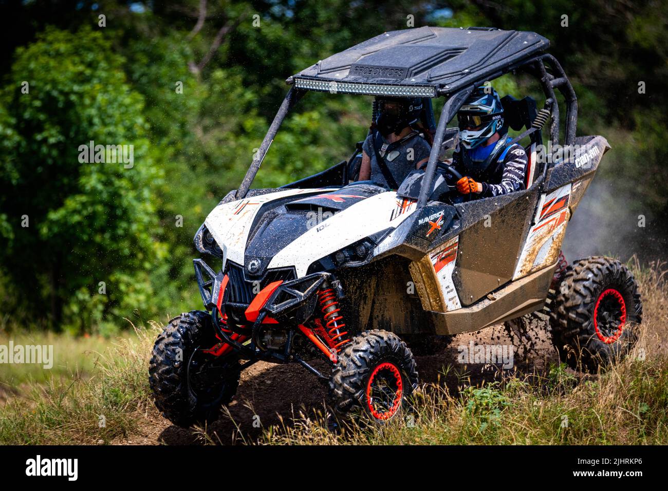 A closeup of drivers in a side-by-side vehicle (UTV) on a dirt track ...