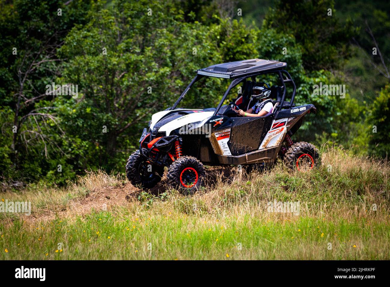 A closeup of a driver in a side-by-side vehicle (UTV) on a dirt track ...