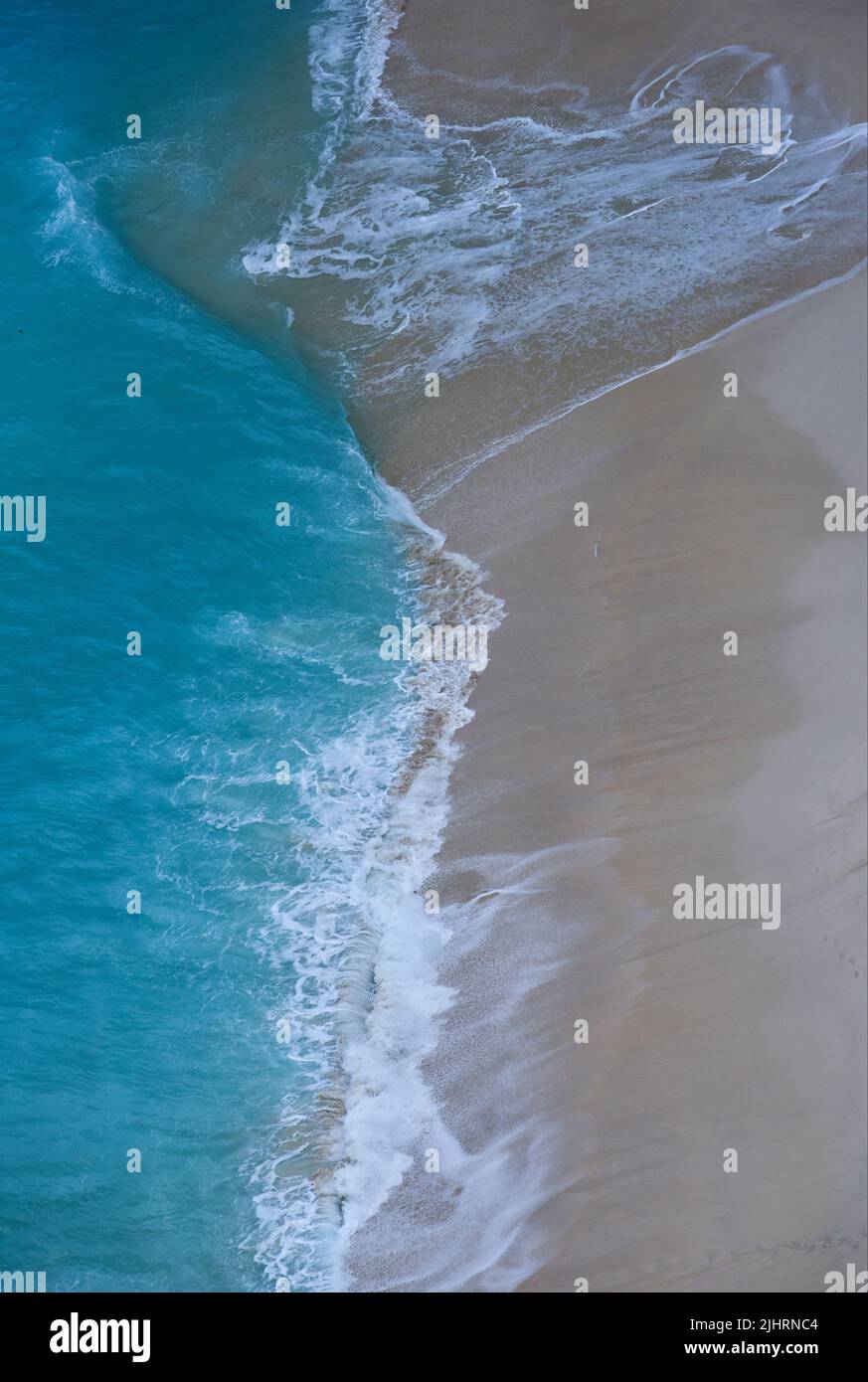 The vertical aerial view of the ocean waves reaching the sandy shore ...