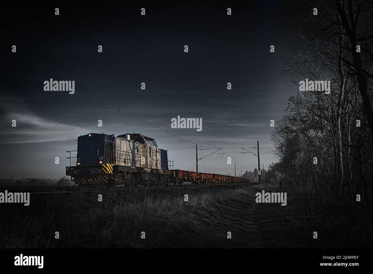 A cargo train on railroads under a gray cloudy sky at night Stock Photo ...