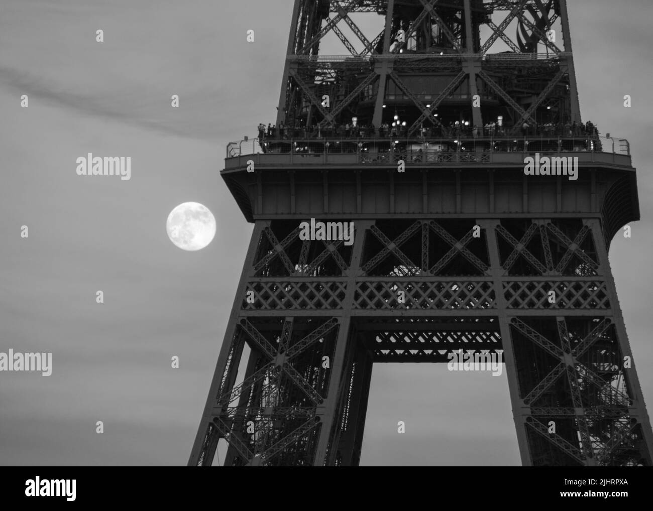 A grayscale shot of the Eiffel tower with the full moon in the ...
