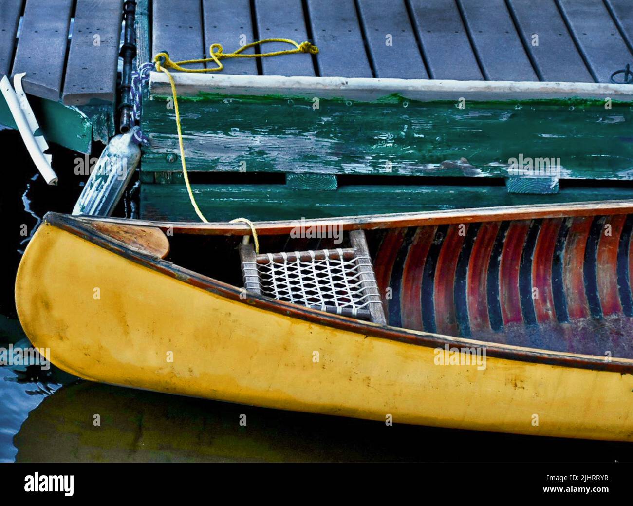 An empty yellow canoe on the lake shore attached to the wooden dock ...