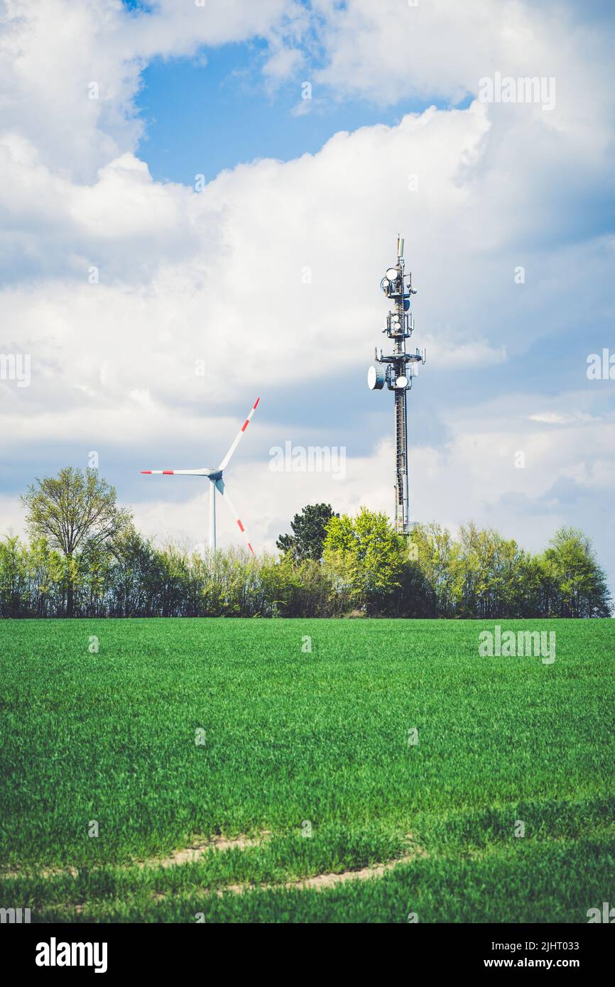 A vertical shot of a wind turbine and a communication tower against a ...