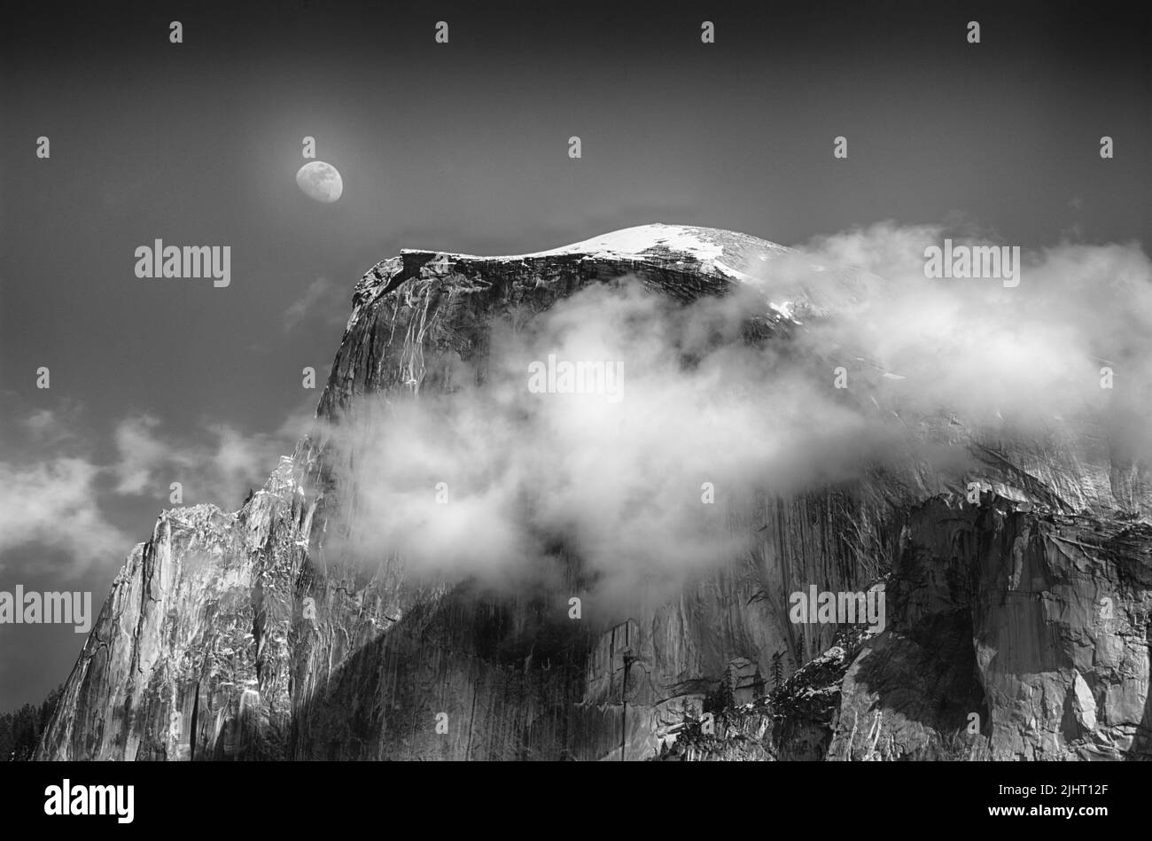 A grayscale of a cloud covered mount peak with the moon in the ...
