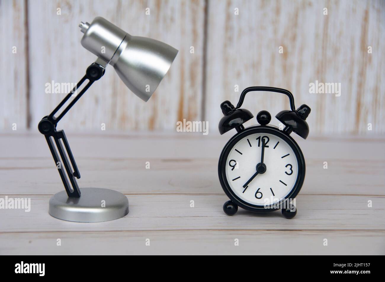 Alarm clock pointing at 7 o'clock with table lamp on wooden background ... Alarm clock pointing at 7 o'clock with table lamp on wooden background ...
