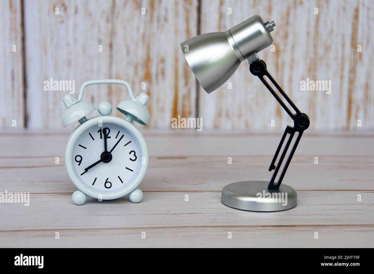 Alarm clock pointing at 8 o'clock with table lamp on wooden background ...
