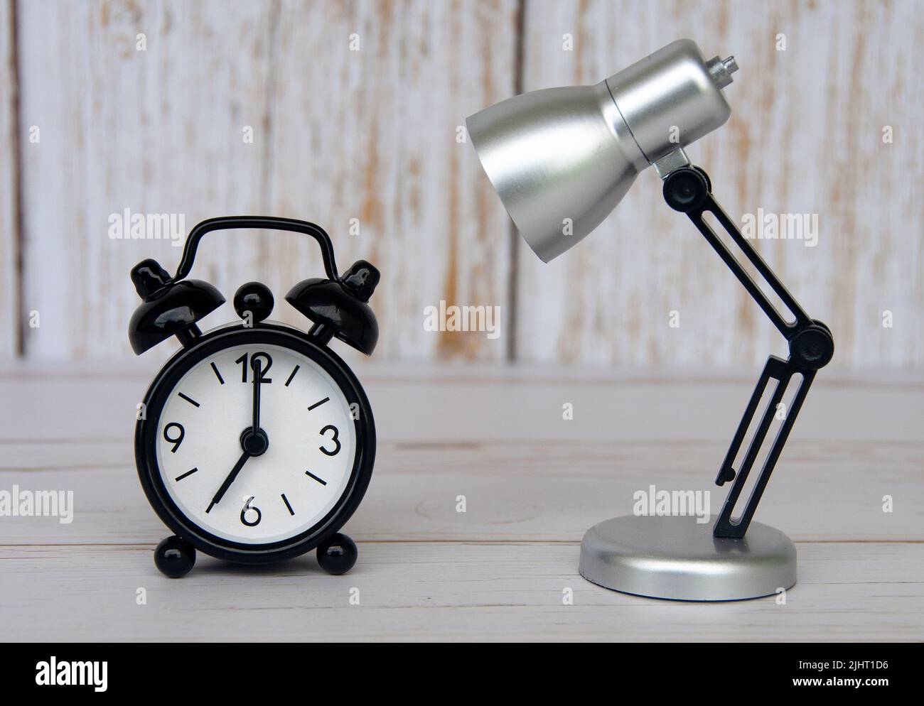Black alarm clock pointing at 7 o'clock with table lamp on wooden ...