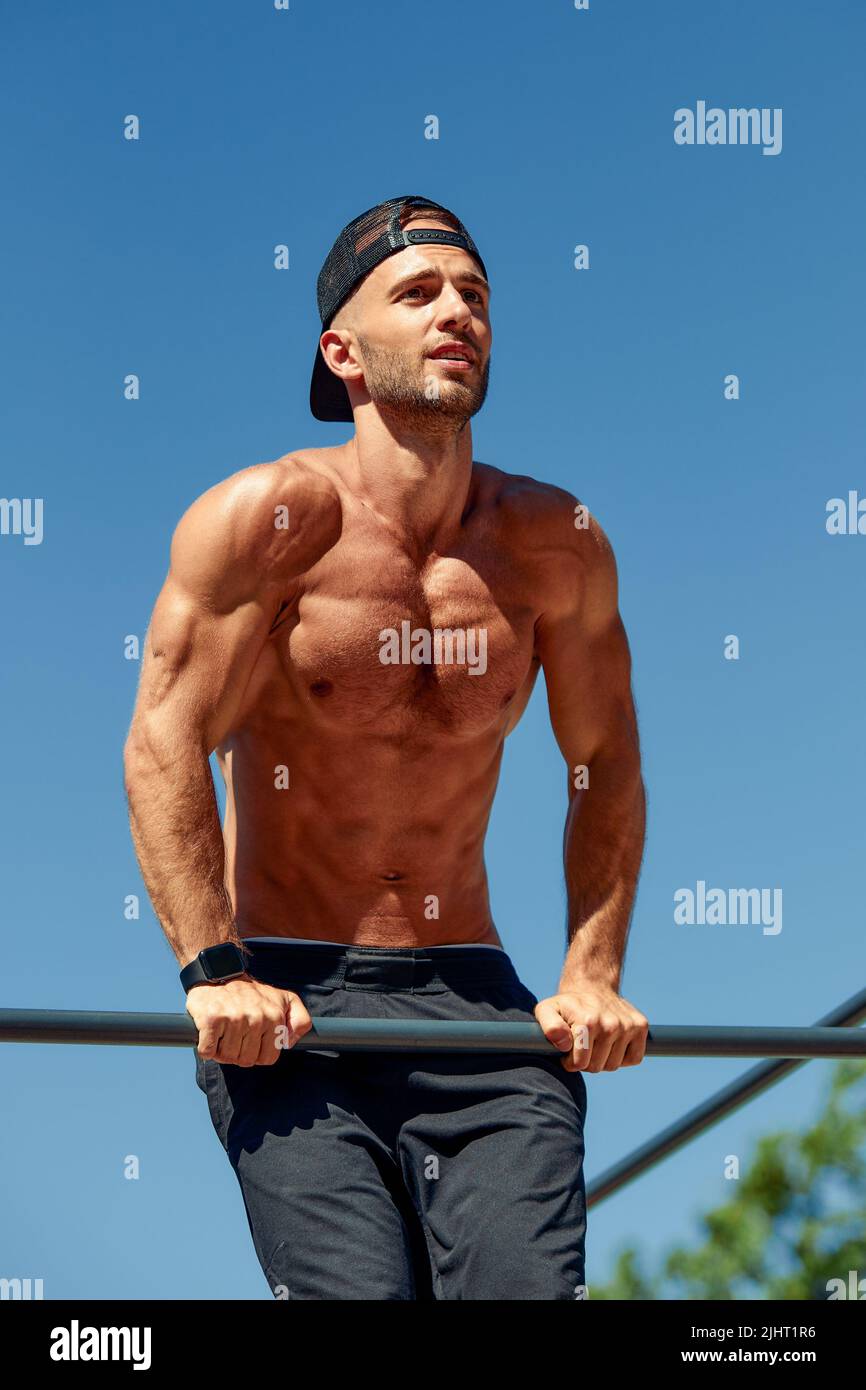 Athletic young man hanging from the bars at the calisthenics gym ...