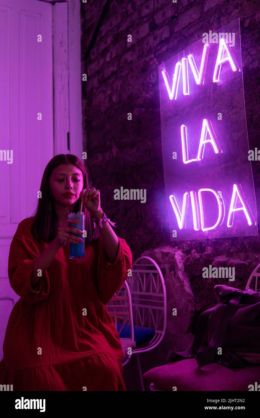 A dark-skinned Hispanic woman dressed in a red outfit stirred her drink ...