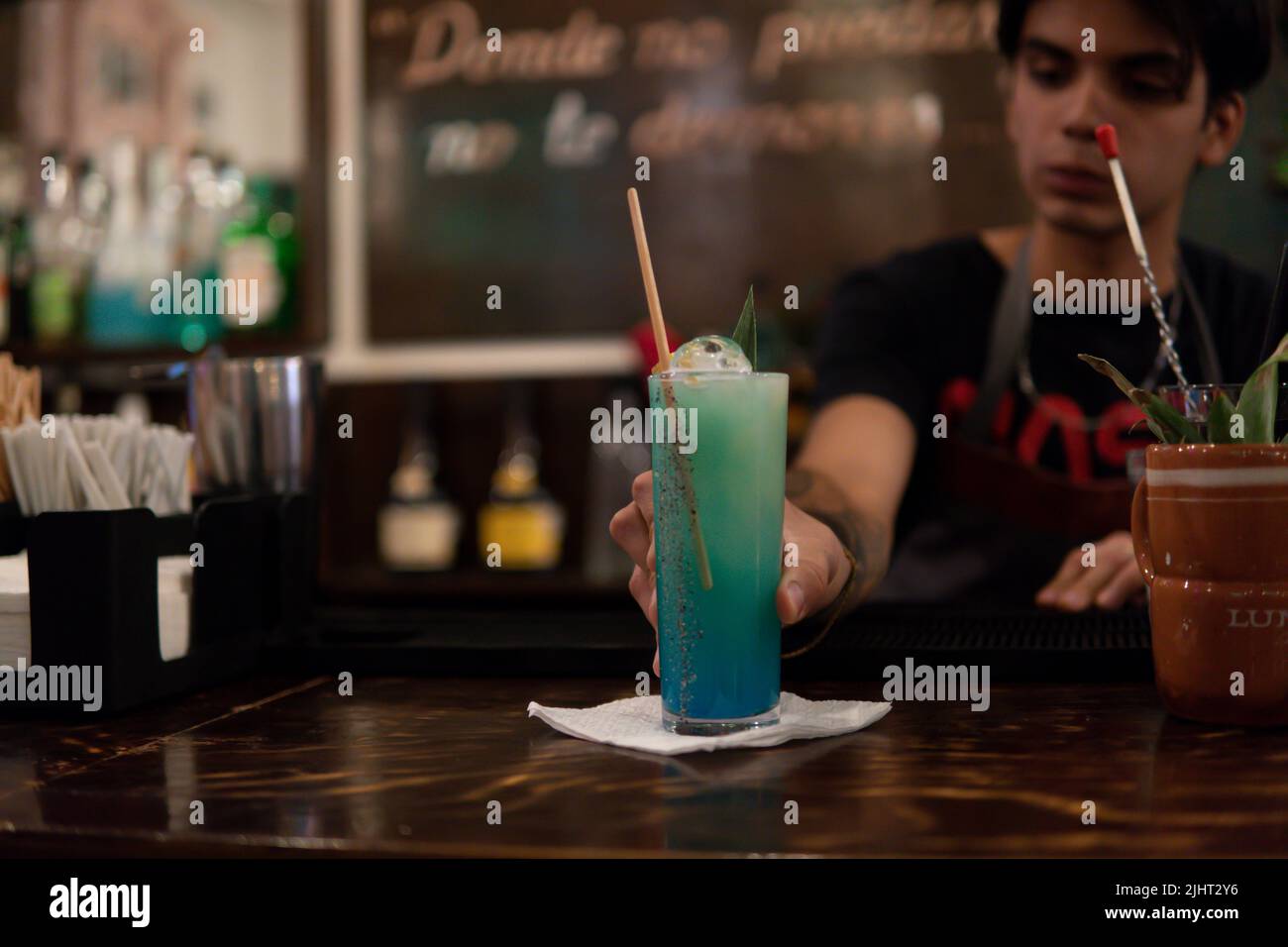 Bartender of a nightclub at the bar counter serving a blue-colored ...