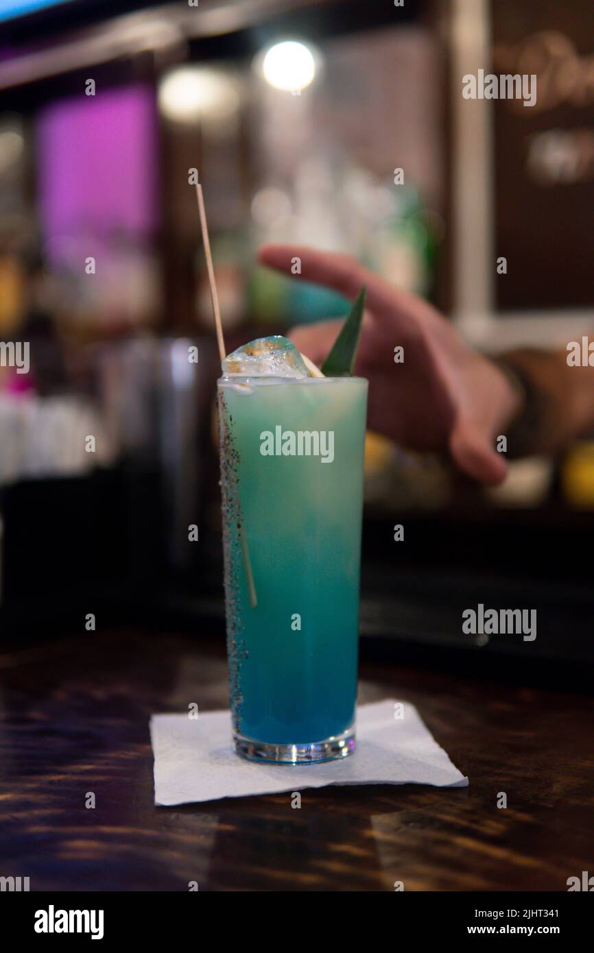 Hand with a blue drink on a bar counter. Waiter serving a colorful ...