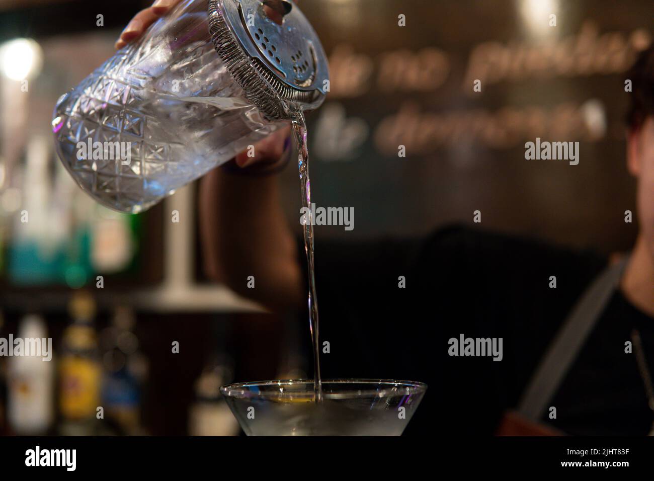 Close-up shot of a bartender's hands pouring the martini shot into a champagne glass. Preparing ...