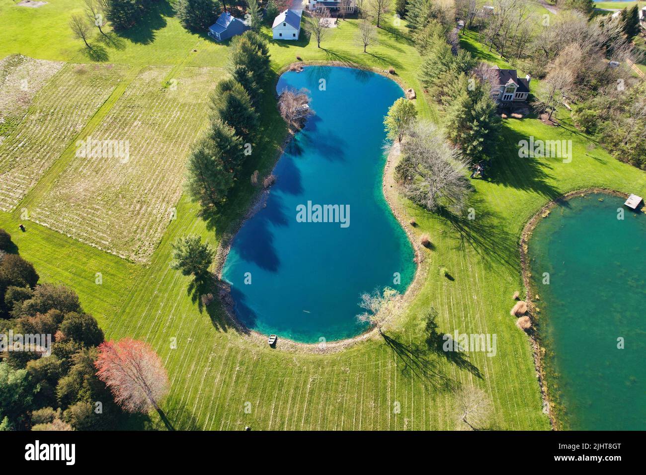 An aerial view of a blue pond in a green field near the houses Stock ...