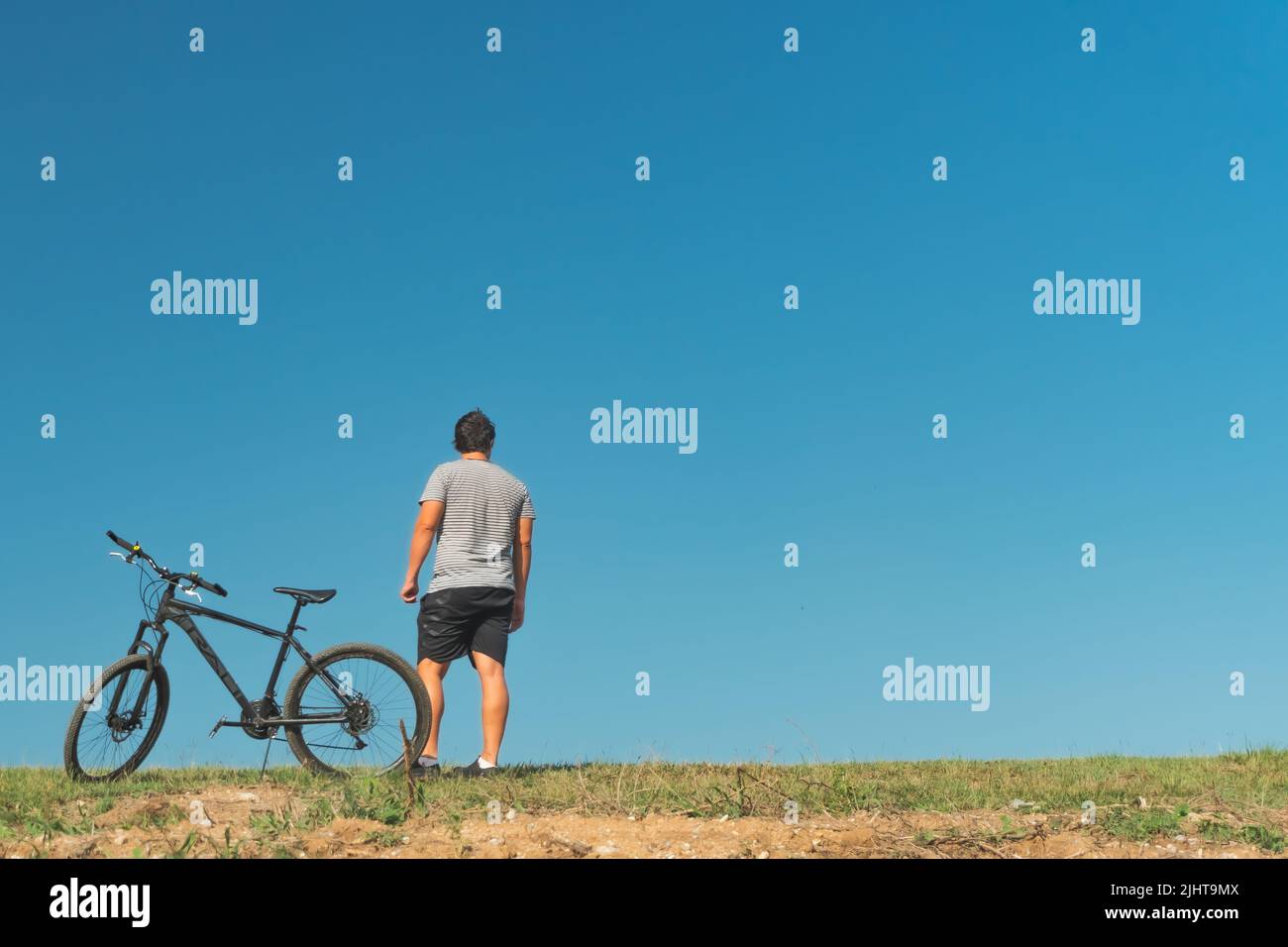 A low-angle shot of the back of a male standing beside a bicycle under ...
