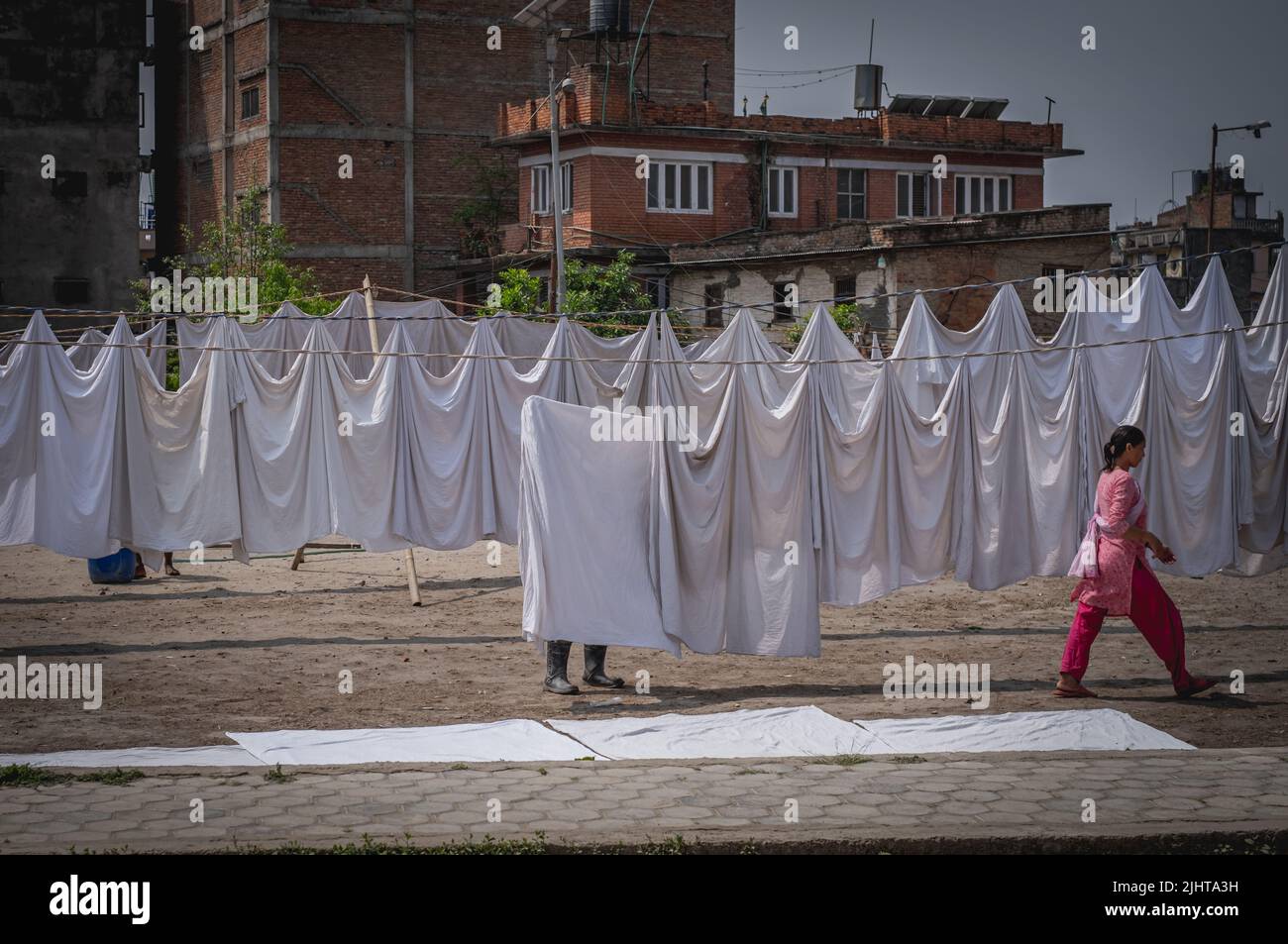 A man hangs up sheets with his legs on display, a woman dressed in pink ...