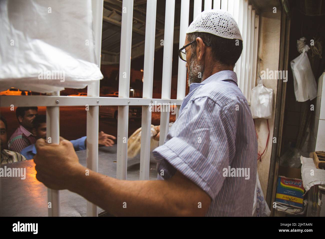 A man serves customers by selling Arabic bread through a barred window ...