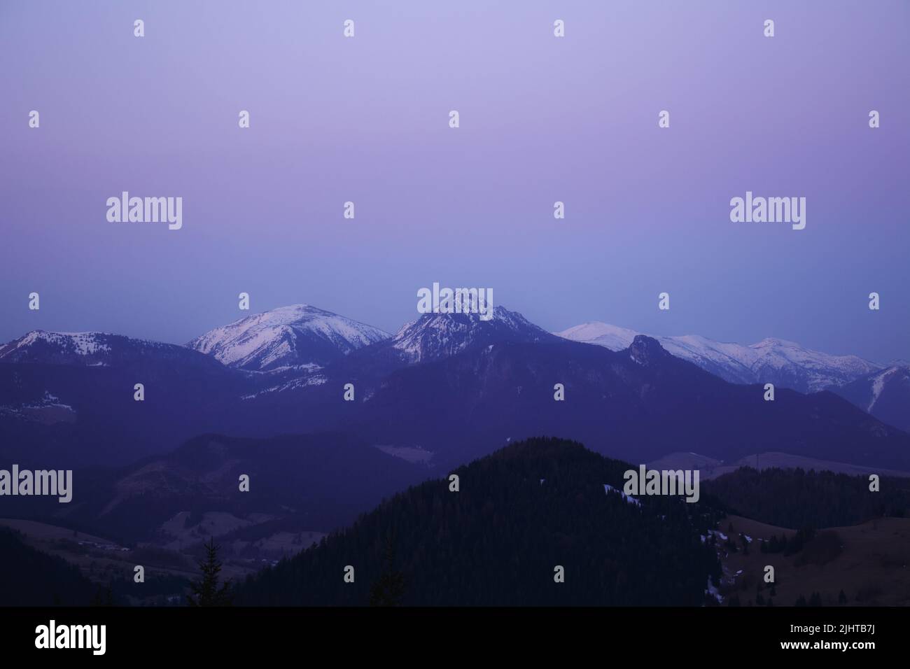A wooded mountains on a snowy mountain range background Stock Photo - Alamy