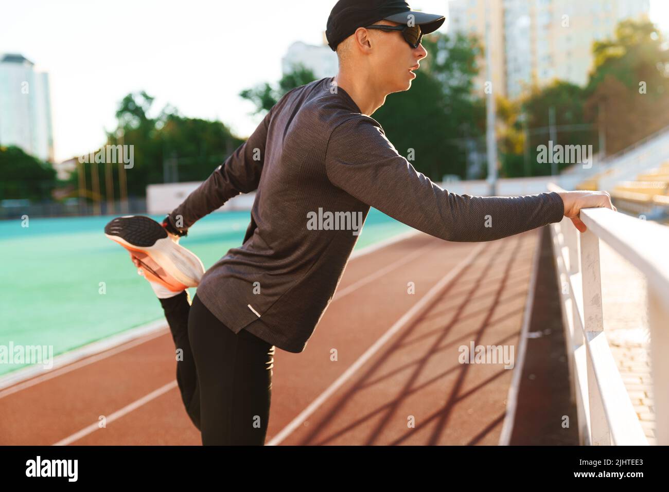 Young white runner doing exercise while working out on stadium outdoors ...