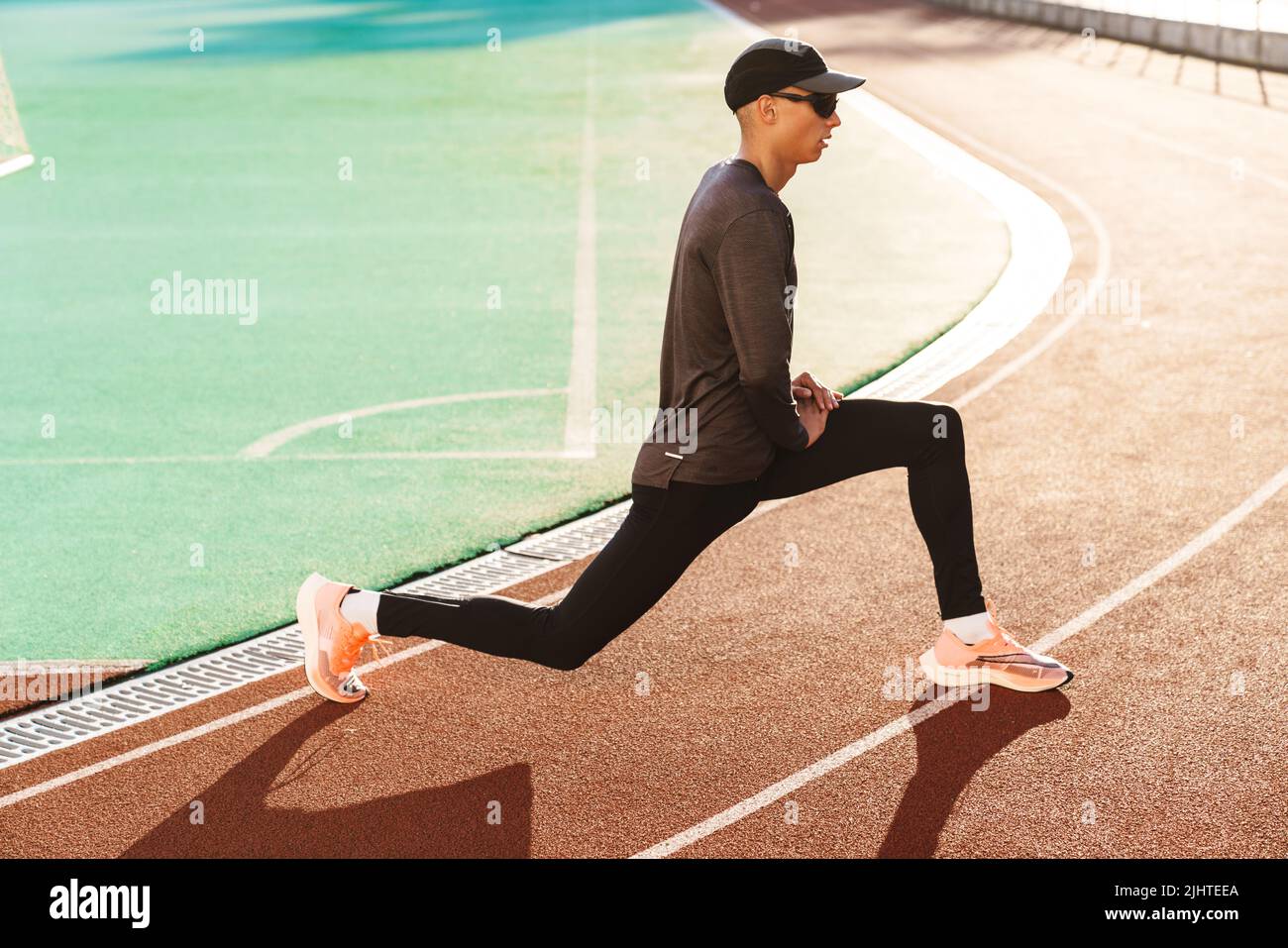 Young white runner doing exercise while working out on stadium outdoors ...