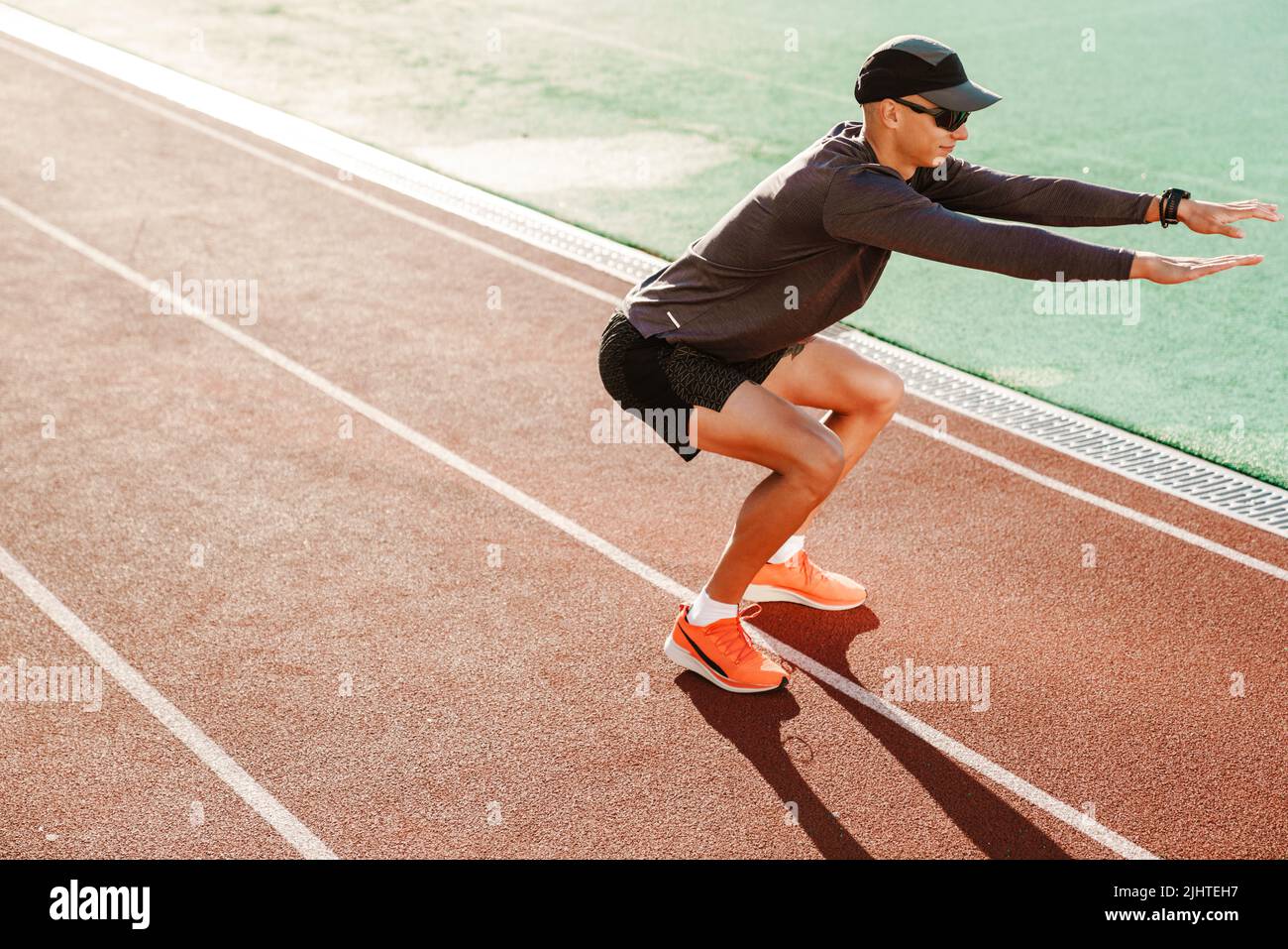 Young white runner doing exercise while working out on stadium outdoors ...