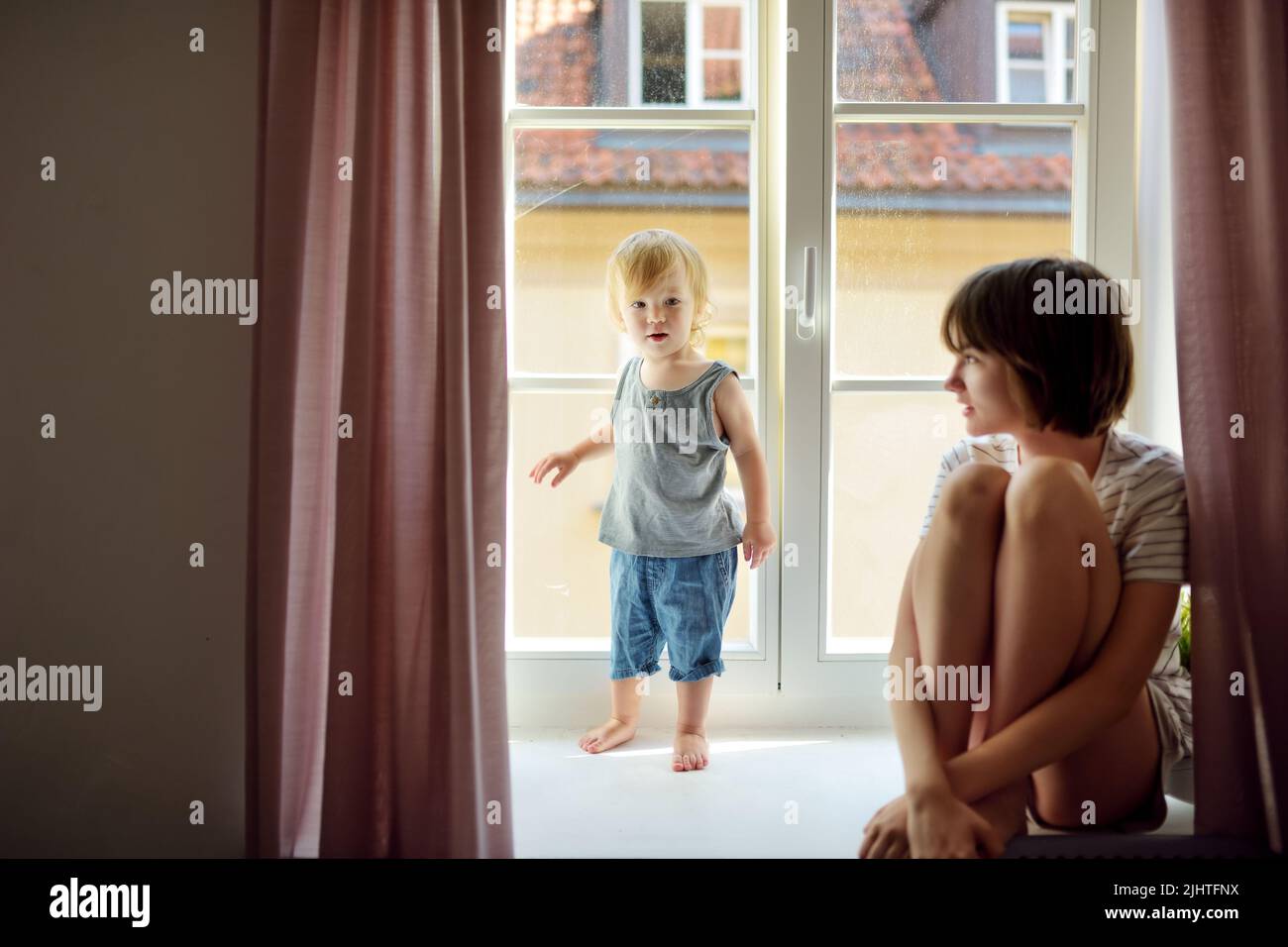 Teenage sister and her toddler brother looking out the window. Siblings ...