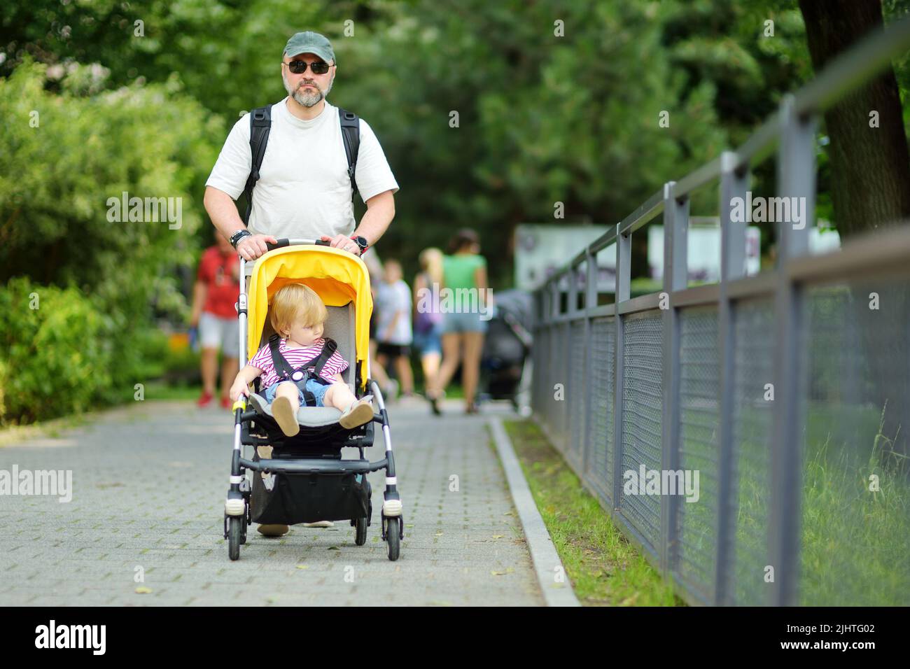 Young father walking in a park with toddler son in pushchair. Man ...