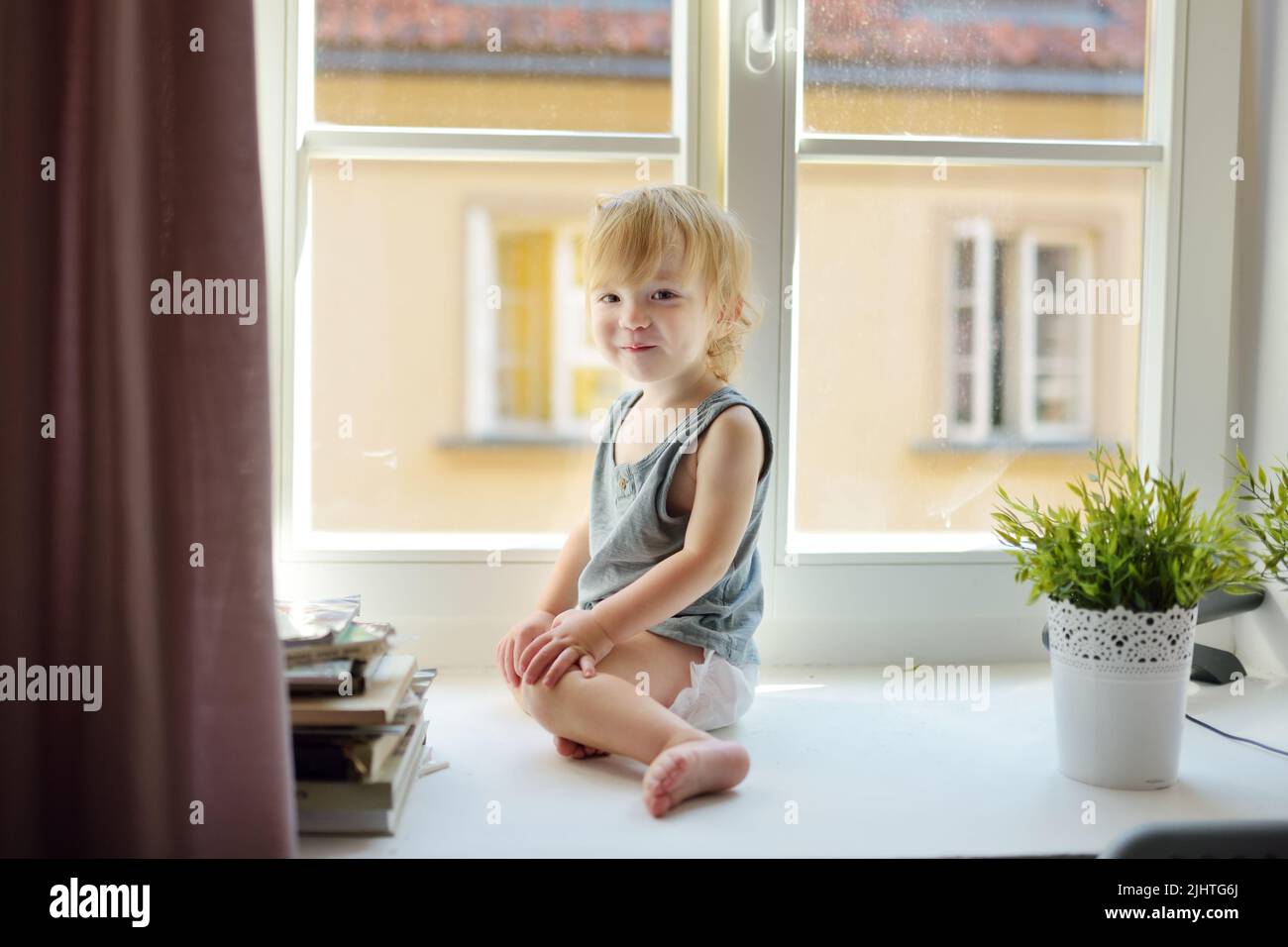 Cute toddler boy standing on a windowsill. Adorable child looking out ...