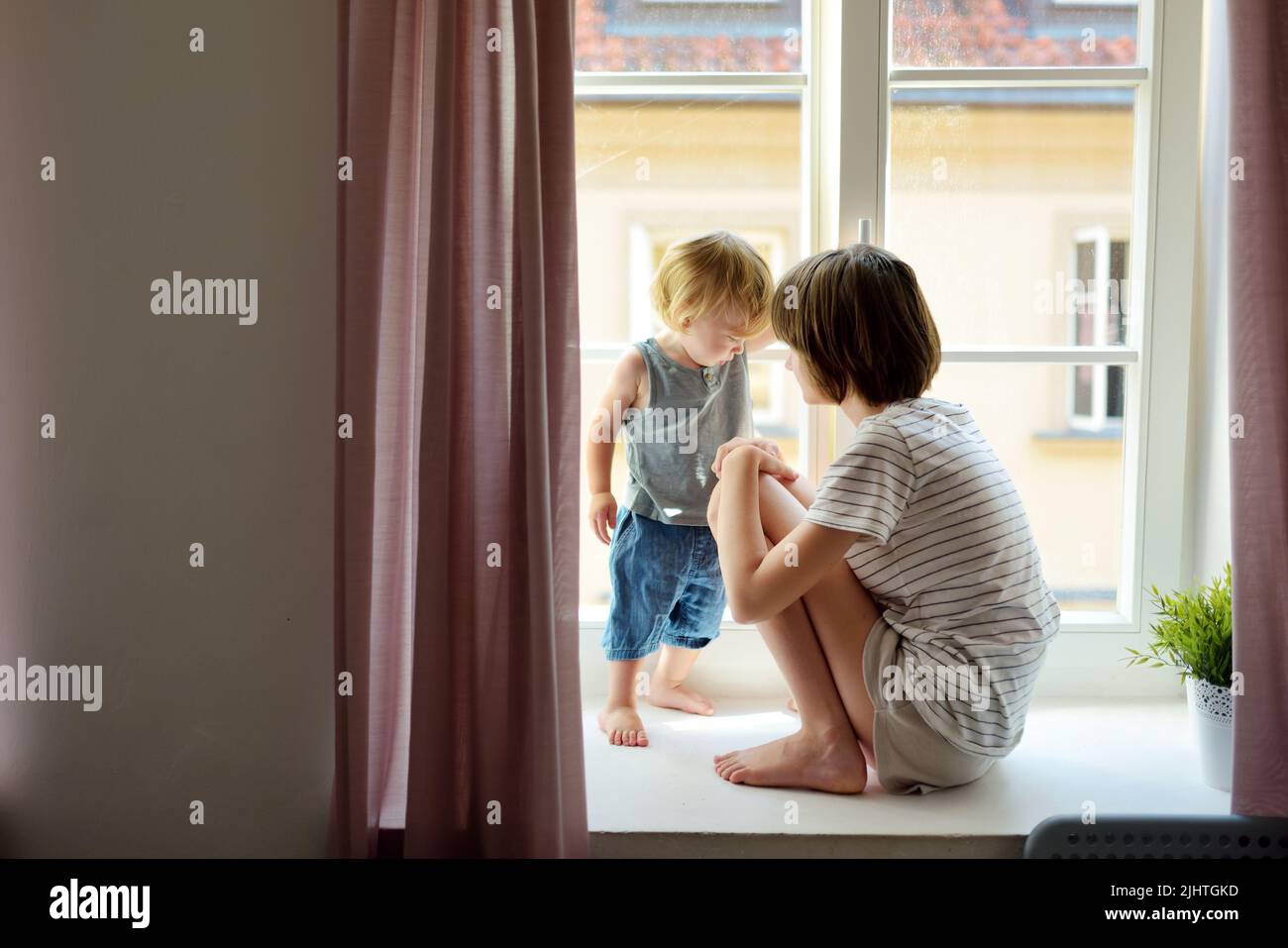 Teenage sister and her toddler brother looking out the window. Siblings ...