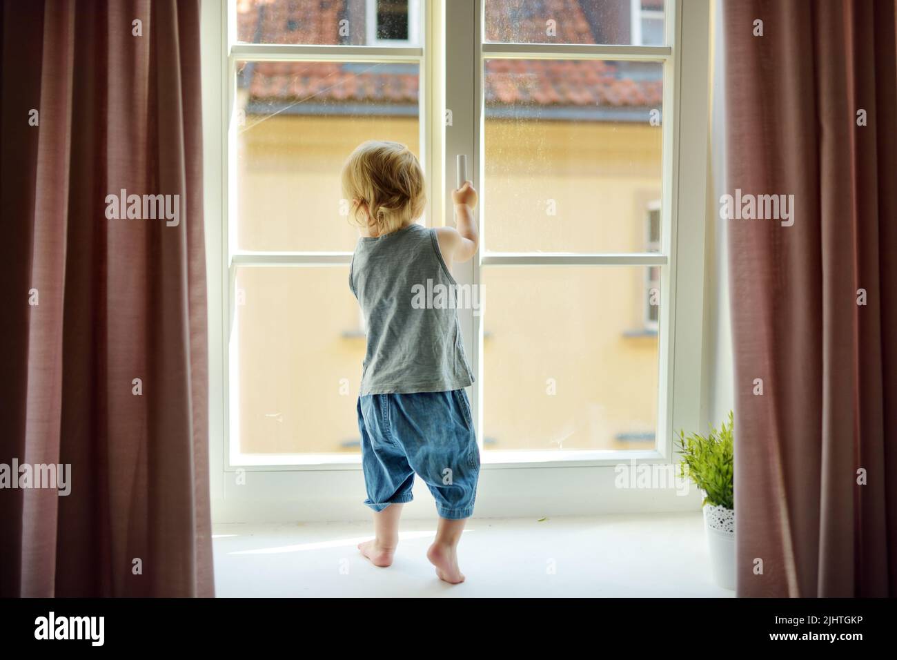 Cute toddler boy standing on a windowsill. Adorable child looking out ...
