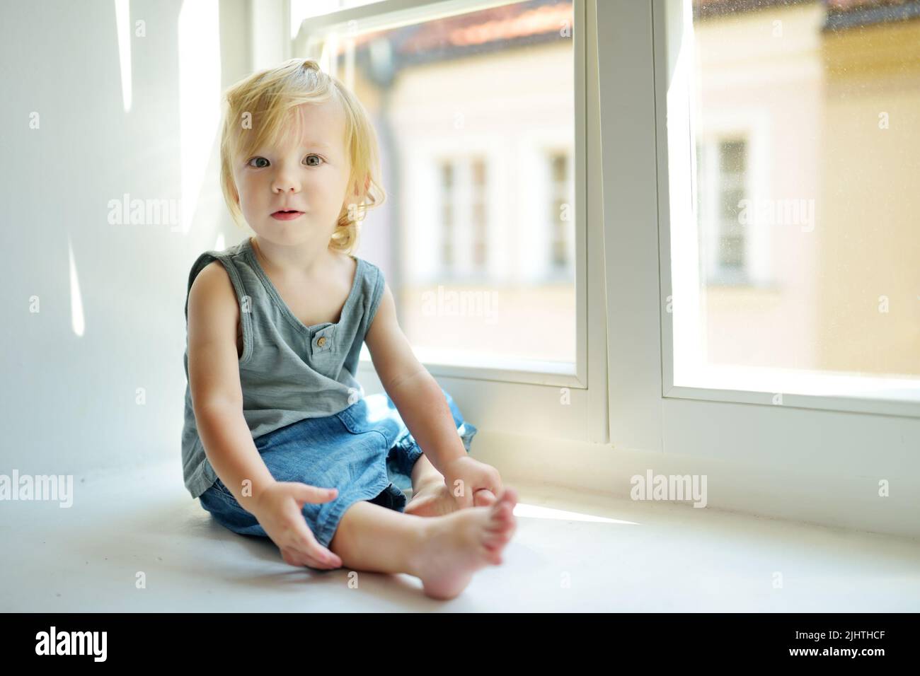 Cute toddler boy standing on a windowsill. Adorable child looking out ...