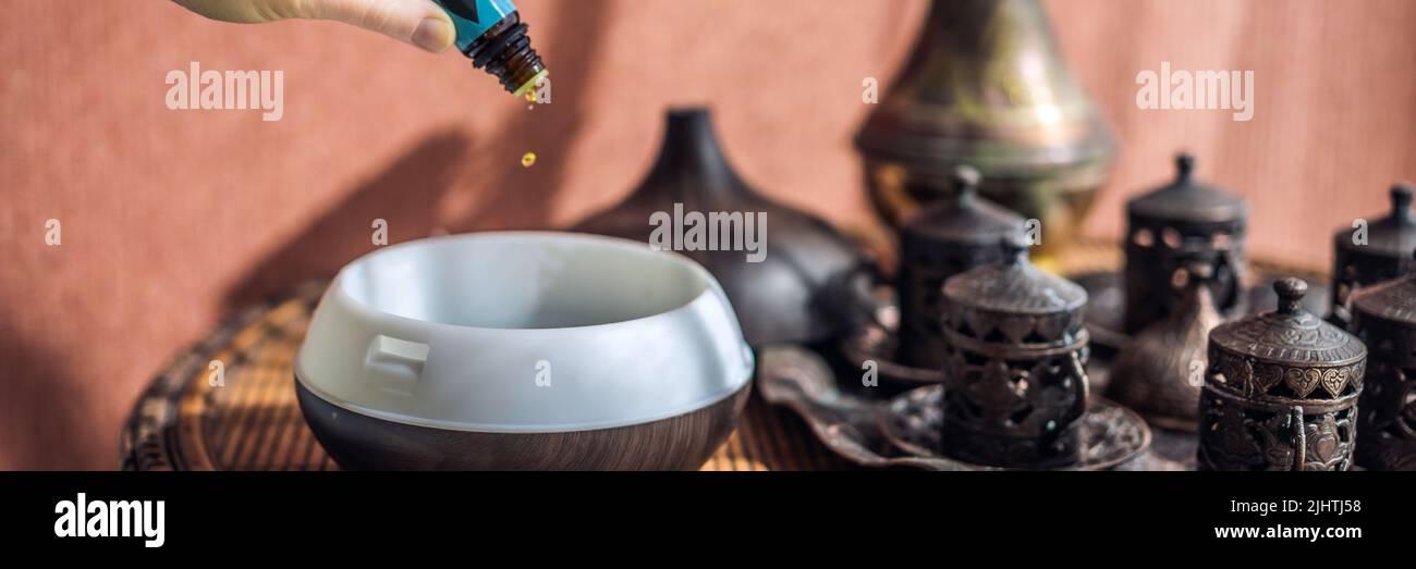 Woman adding essential oil to aroma diffuser on table BANNER, LONG ...