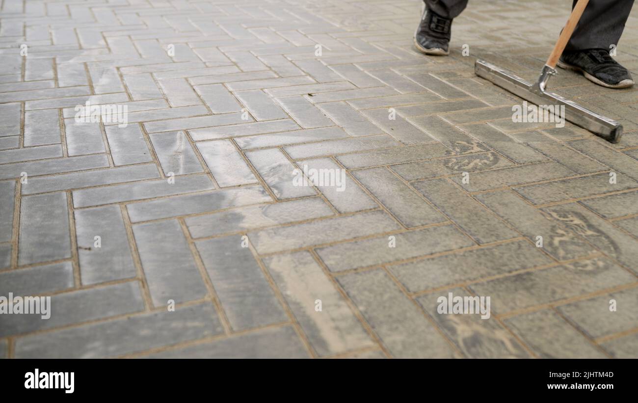 The concept of laying paving stones. A worker using a mop rubs the sand ...