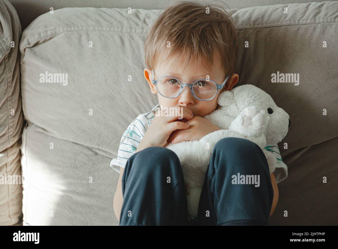 A child with autism in glasses sits on the sofa and sad, hug a s Stock ...