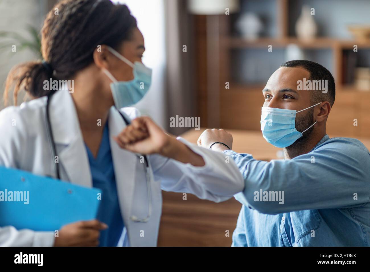 Black woman doctor greeting male patient with elbow touch Stock Photo ...
