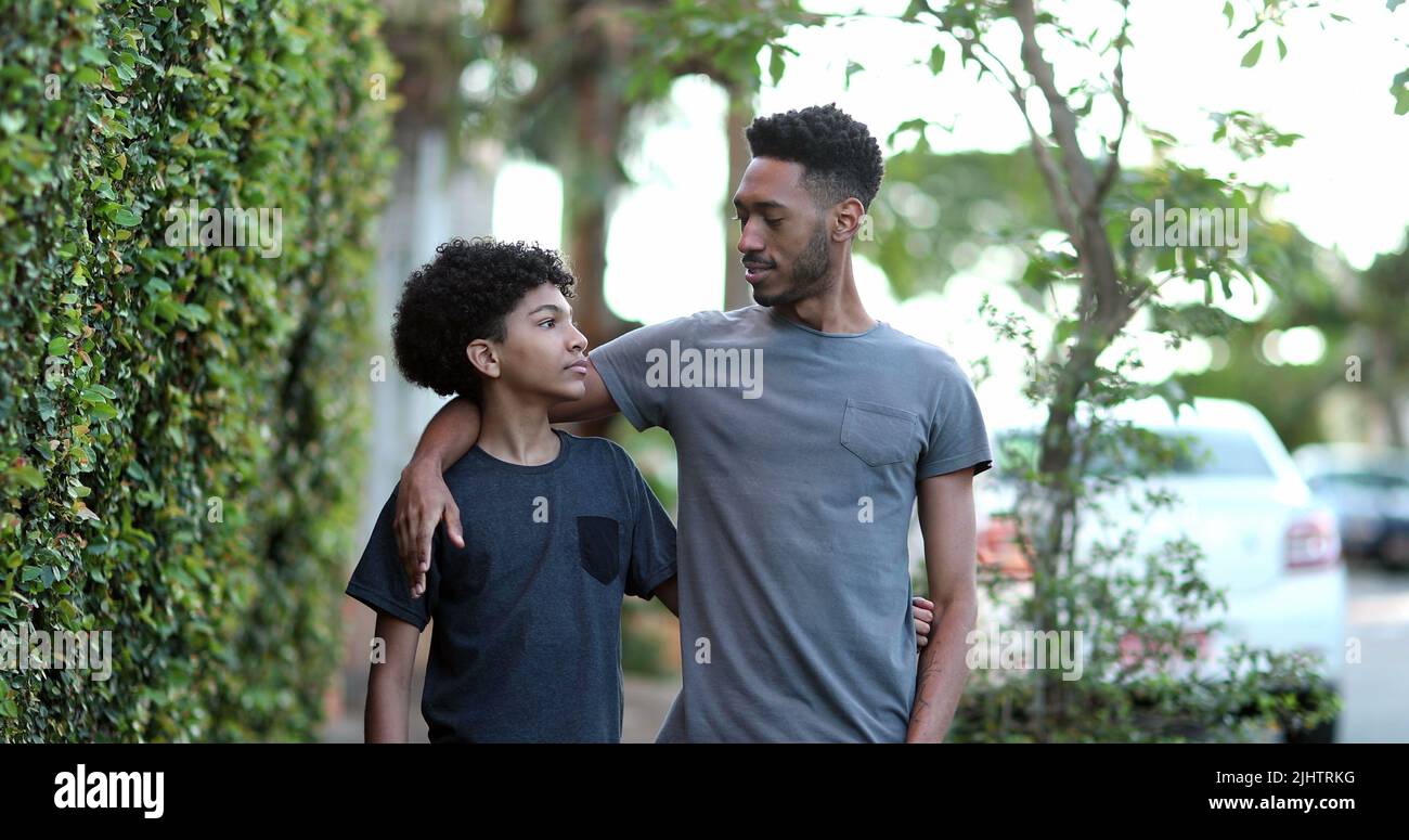 Two brothers walking together in sidewalk. Black brother giving advice ...