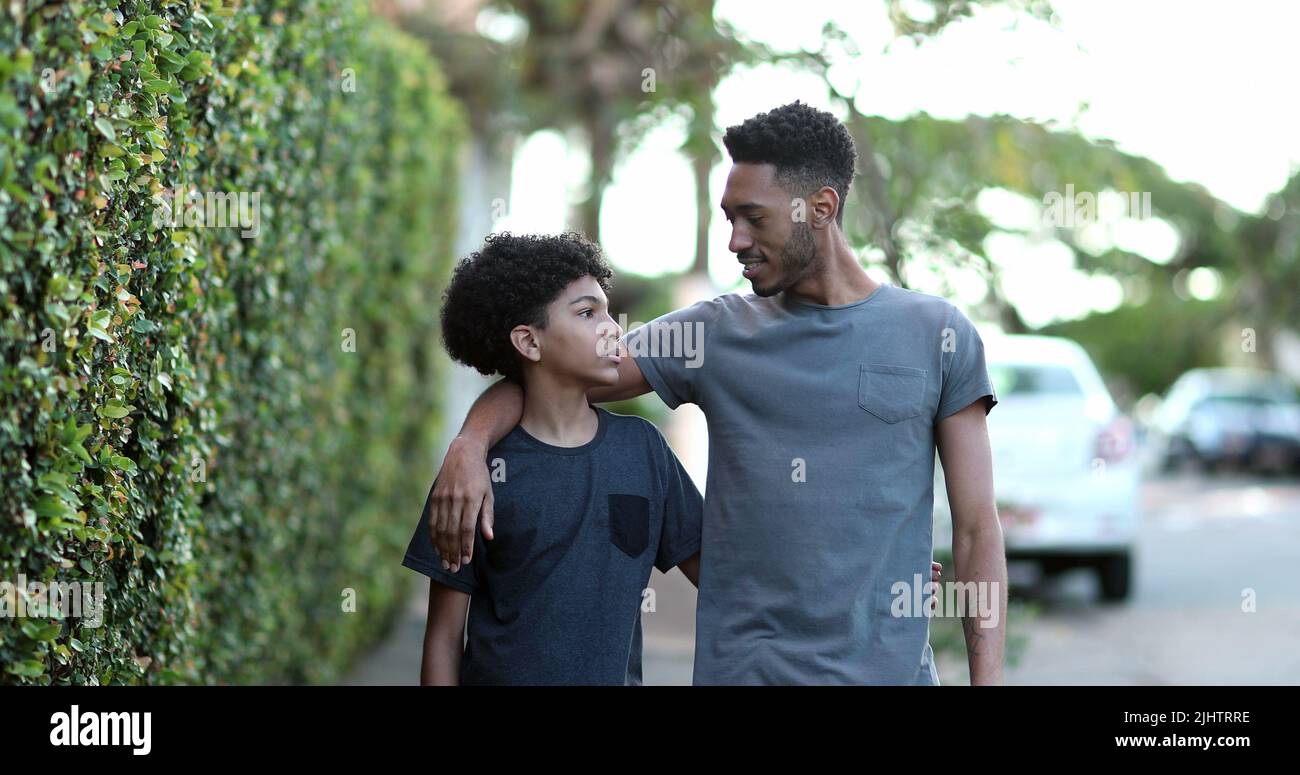 Two brothers walking together in sidewalk. Black brother giving advice ...