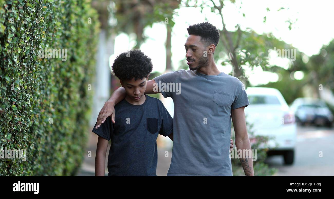 Two brothers walking together in sidewalk. Black brother giving advice ...