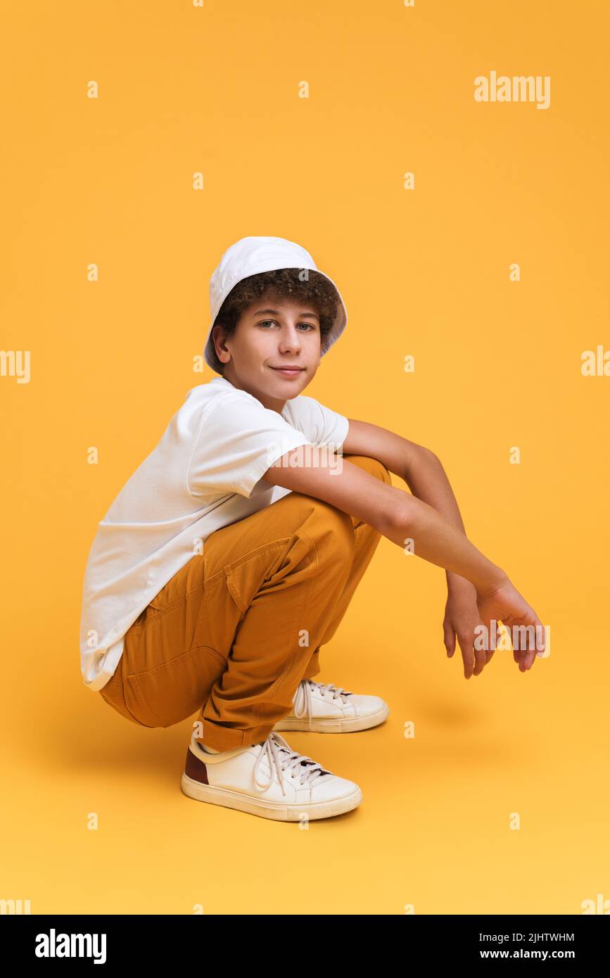White curly boy wearing panama smiling while squatting isolated over ...
