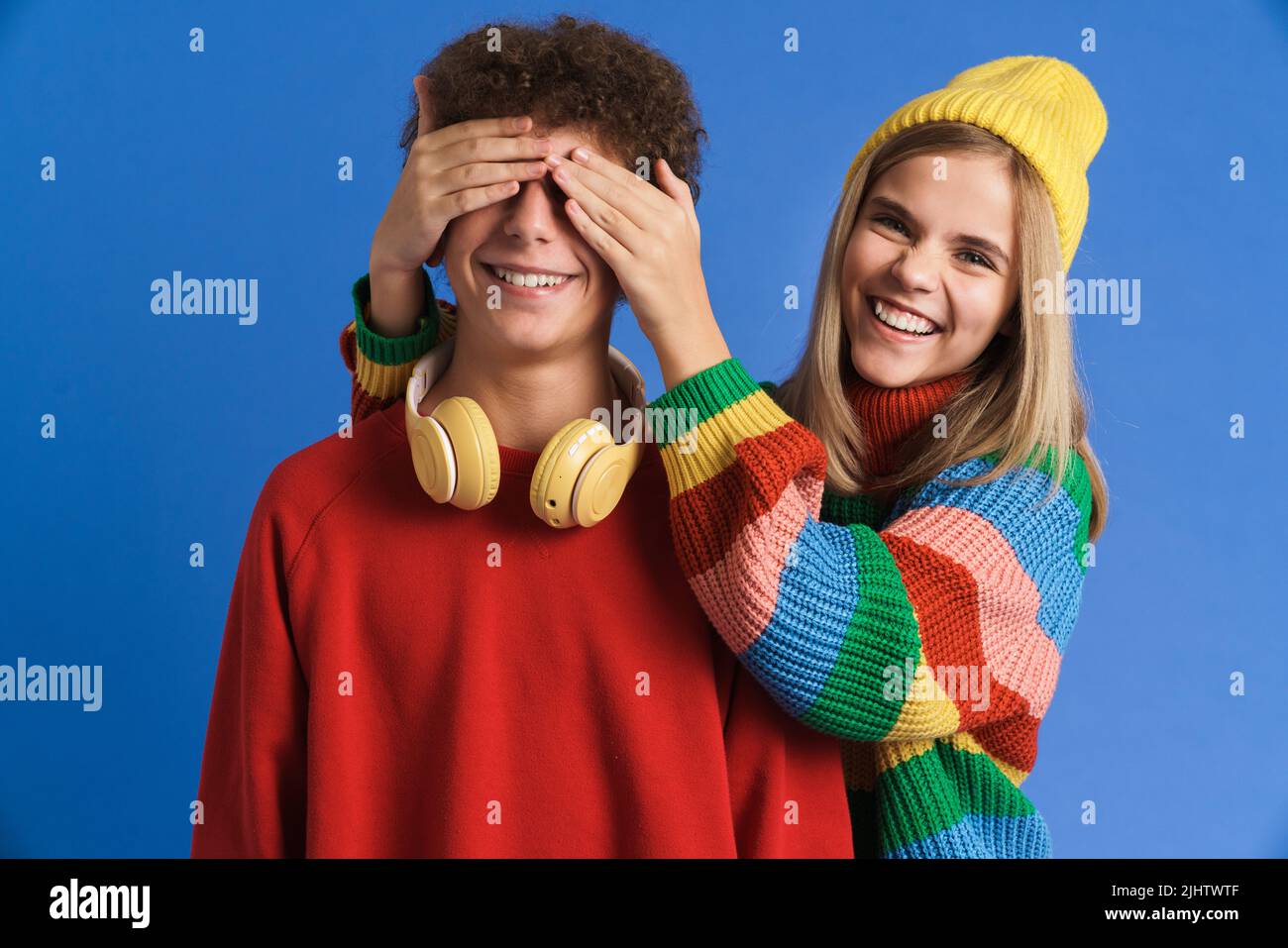 White girl wearing hat covering her friend's eyes and laughing isolated ...