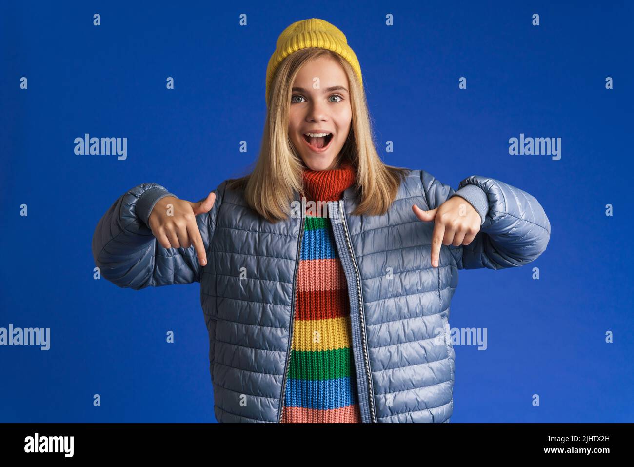 White girl wearing hat smiling and pointing fingers downward isolated ...